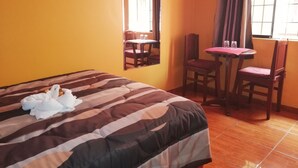 Quarto de hotel com cama, uma pequena mesa com cadeiras, janela com cortinas e um espelho na parede.
