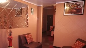 Um hall com carpete vermelho, dois sofás marrons com almofadas estampadas, um painel decorativo e um quadro emoldurado.
