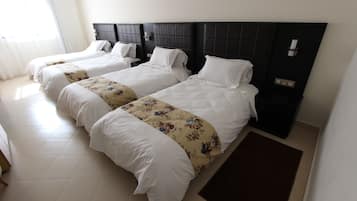 Quarto de hotel com três camas de solteiro, uma cabeceira escura e um tapete marrom.