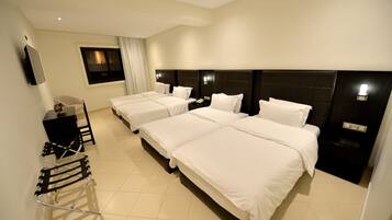 Quarto de hotel com três camas, uma escrivaninha, uma cadeira e uma televisão.