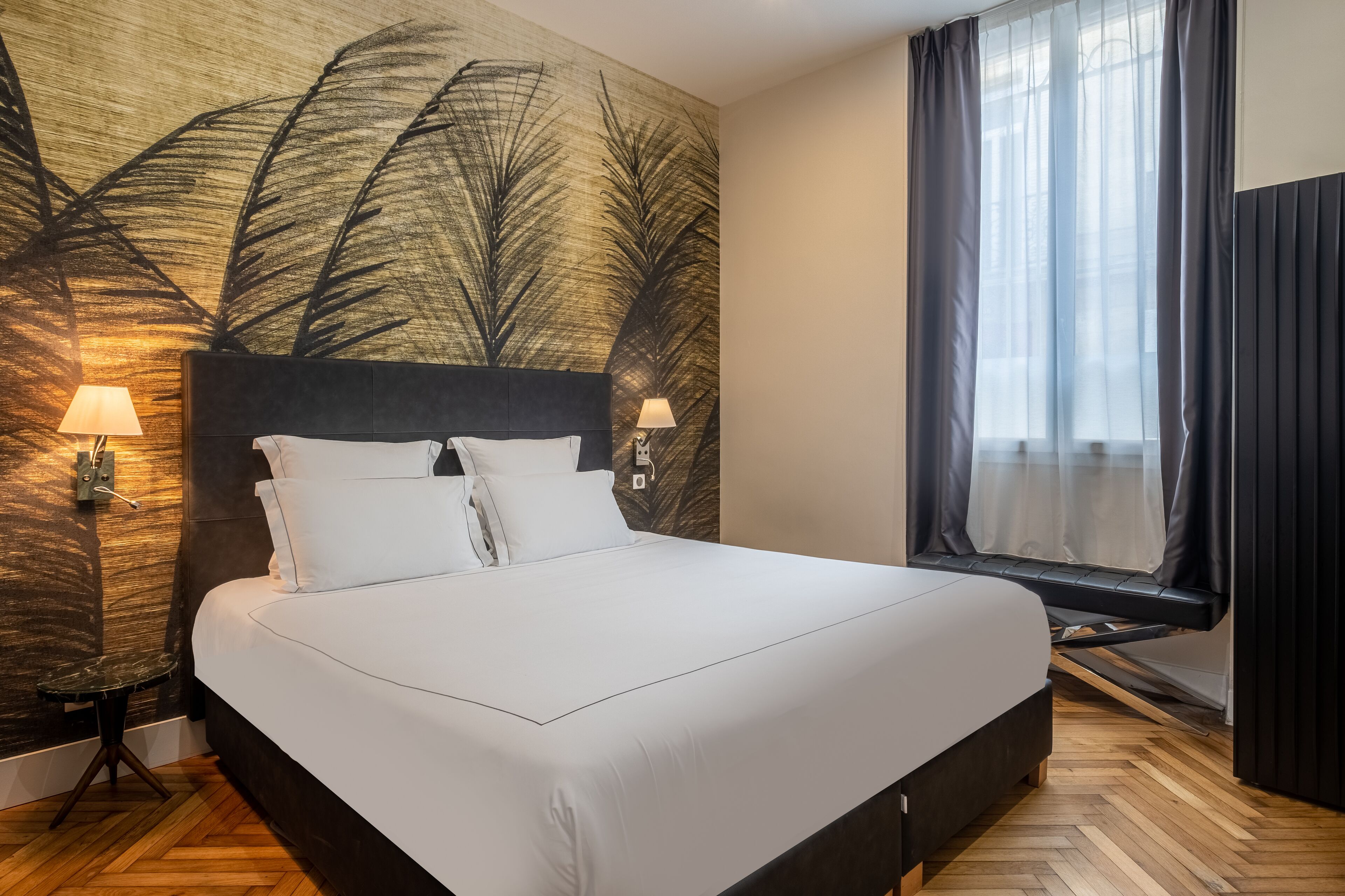 Uma cama bem arrumada com cabeceira, duas luminárias de apoio e uma parede com padrão de folhas.