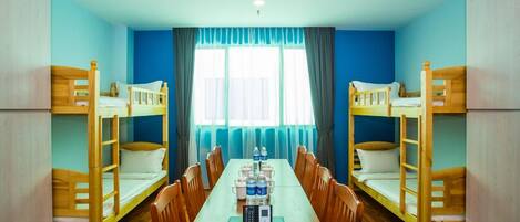 Quarto com beliches de ambos os lados de uma mesa central, uma janela com cortinas e uma luminária no teto.