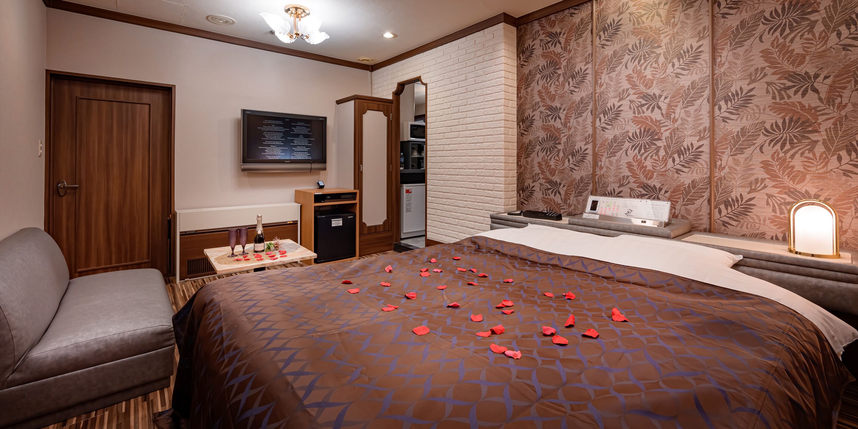 Quarto de hotel com cama, sofá, escrivaninha com computador, televisão e minibar.