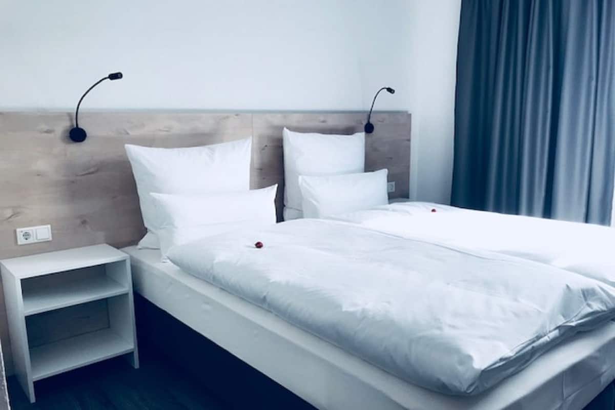 Uma cama de casal com roupa de cama branca, cabeceira de madeira, mesas de cabeceira e mesa de apoio.