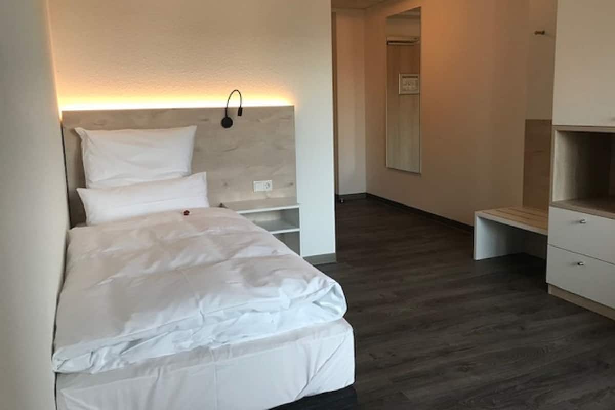 Quarto de hotel moderno com cama bem arrumada, estantes embutidas e closet espaçoso.