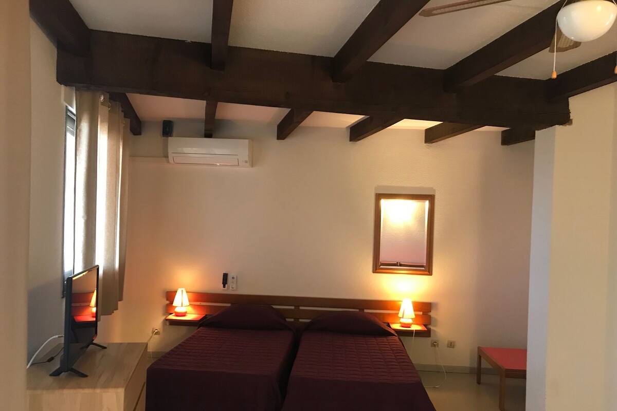 Quarto com duas camas, mesa de cabeceira com luminárias, espelho e janela.