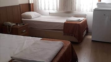 Quarto de hotel com duas camas de solteiro, uma mesa de cabeceira com telefone, uma pequena mesa com um caderno, um radiador e um frigorífico.