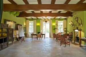 Um quarto espaçoso com soalho de pedra, vigas de madeira, um candelabro, um espaço de refeições com cadeiras riscadas e uma lareira.