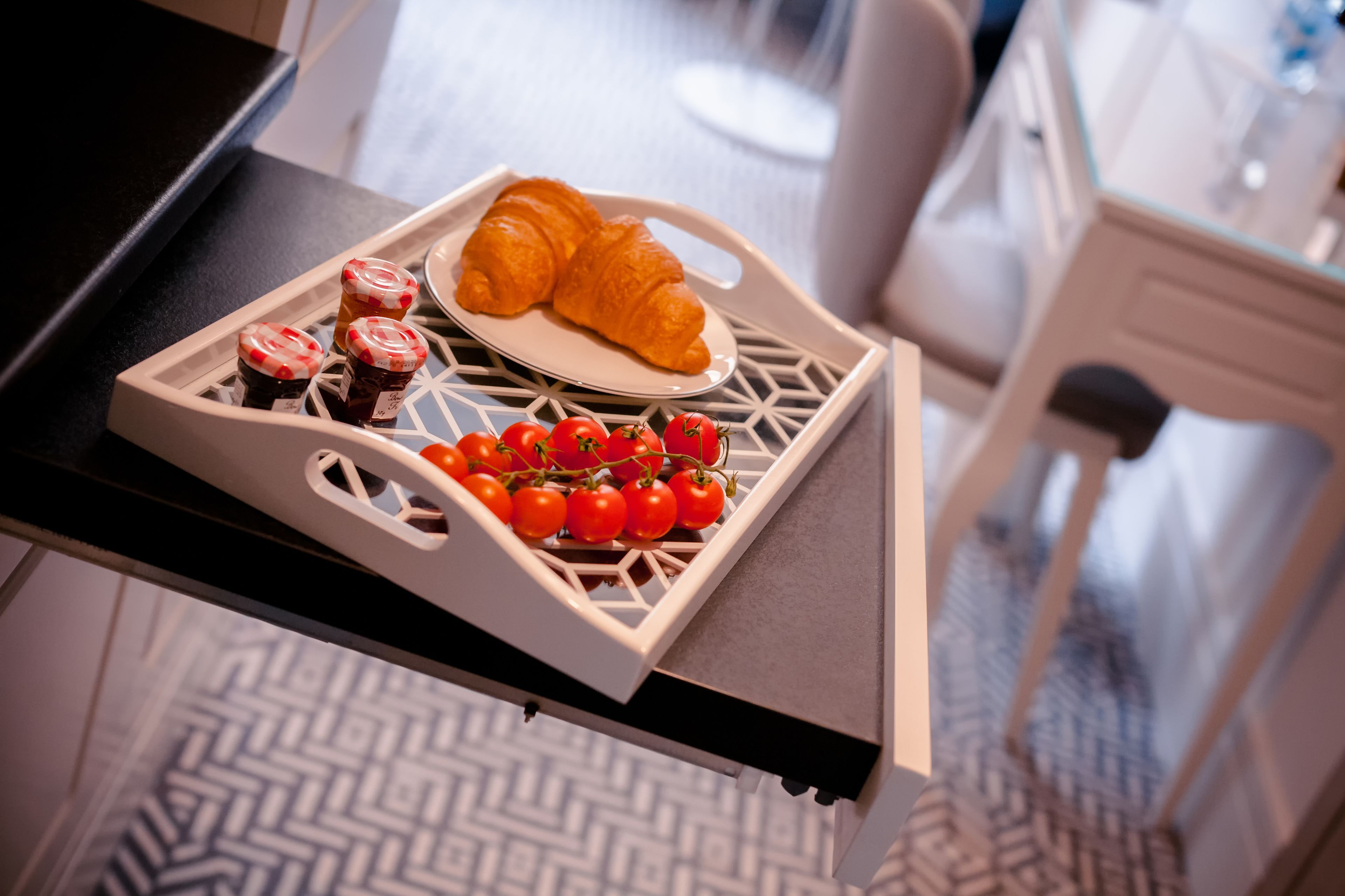 Uma bandeja com croissants, geleia e tomates sobre uma mesa em quarto de hotel.