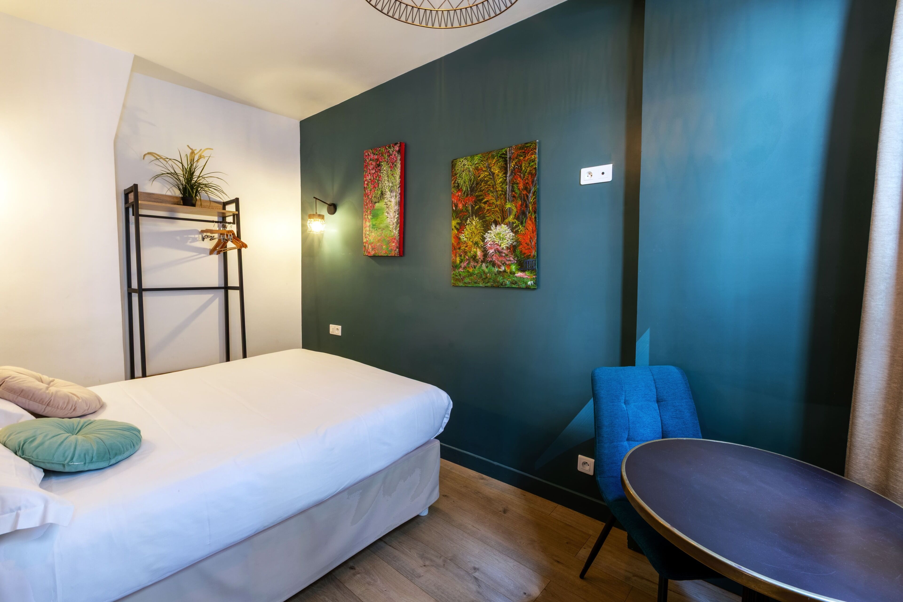Um quarto com uma cama, uma cadeira azul e duas pinturas na parede.