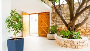 Um espaço amplo em ambiente interno com uma grande árvore, uma porta de madeira e uma parede de pedra.