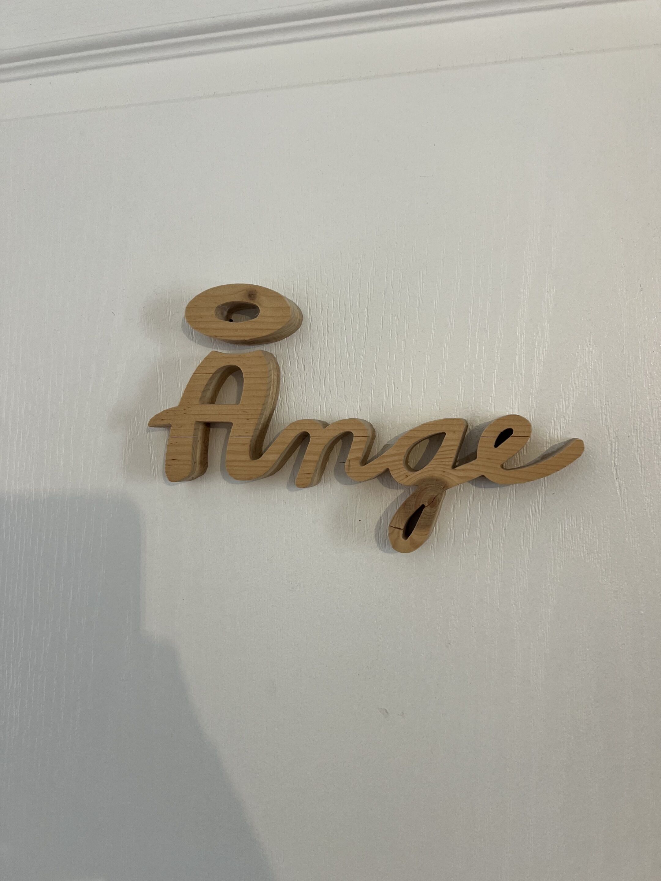 Uma placa de madeira com a palavra 'Ange' numa parede branca.