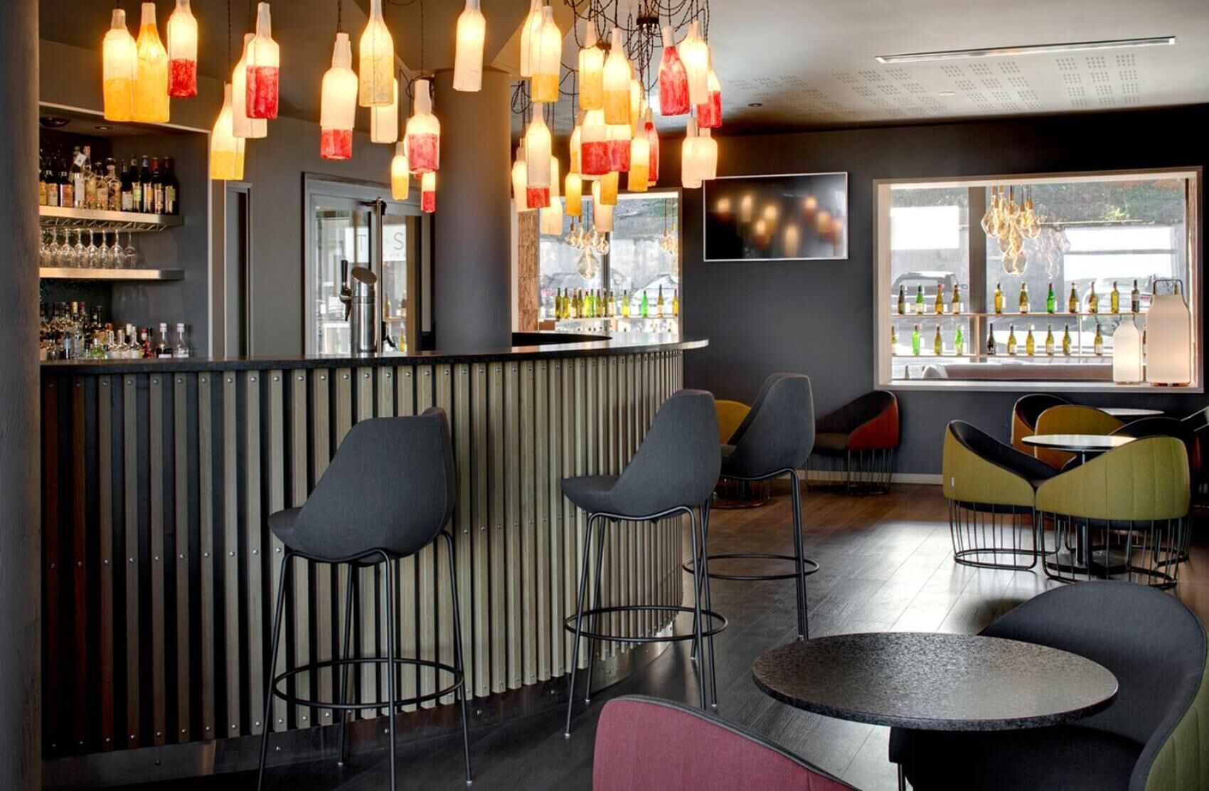 Uma área de bar moderna com balcão, banquetas e luminárias pendentes.