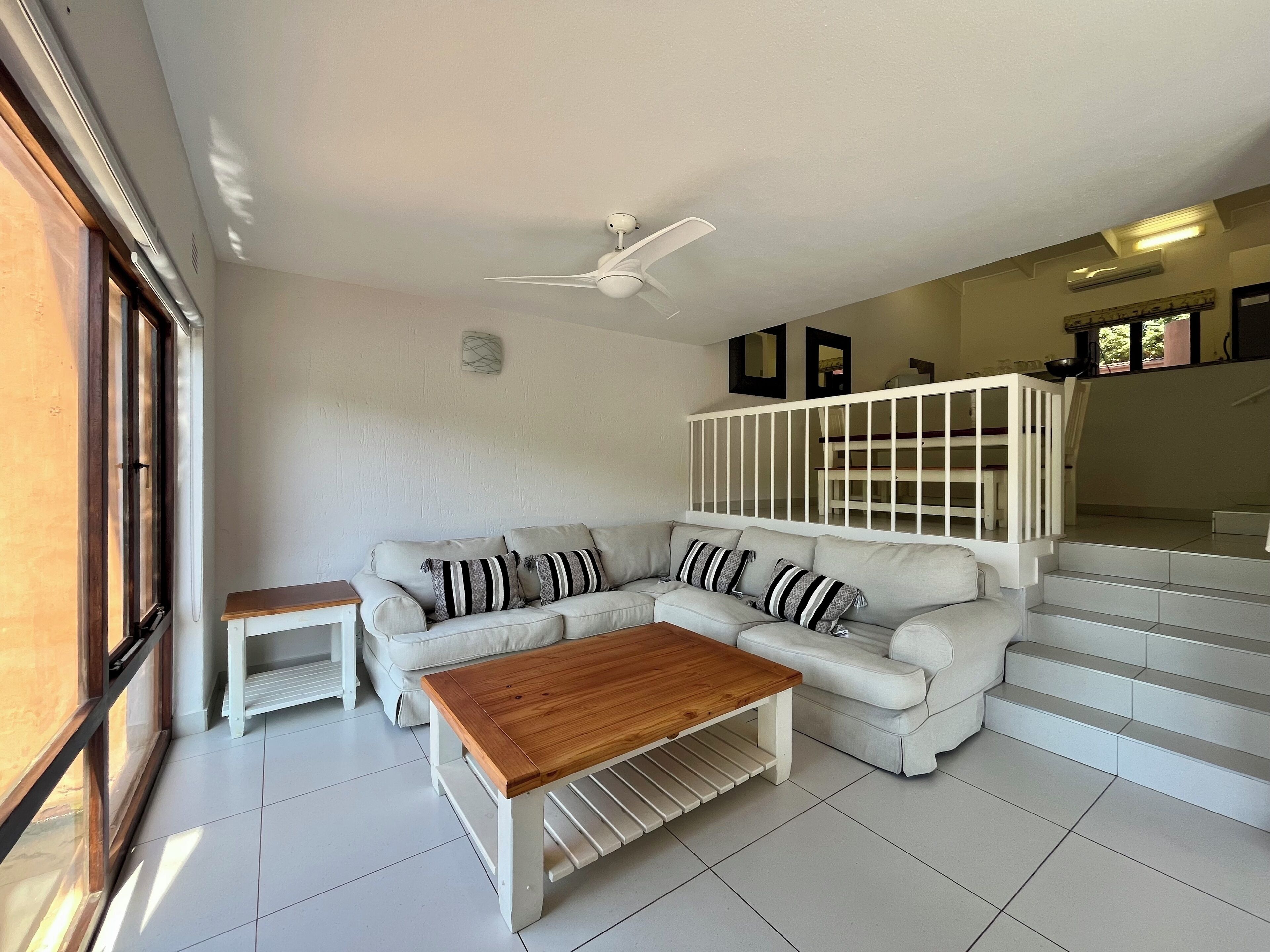 Uma sala de estar com um sofá branco, uma mesa de centro de madeira, uma poltrona branca e uma escada branca.