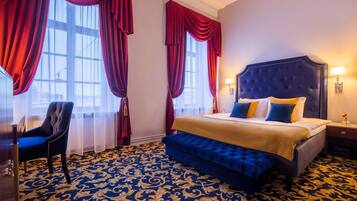 Quarto de hotel com uma cama grande, uma poltrona estofada em azul e um tapete estampado.