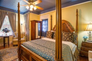 Uma cama com dossel e cortina, um criado-mudo de madeira, uma cadeira e uma escrivaninha com abajur.