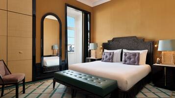 Quarto de hotel com uma cama grande, um banco, uma cadeira, um espelho e duas mesas de cabeceira com abajures.