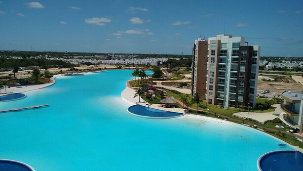 Um resort com várias piscinas, um edifício grande com varandas e um céu azul límpido.