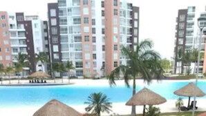 Varanda com duas cadeiras e uma mesa, com vista para uma piscina e palmeiras.