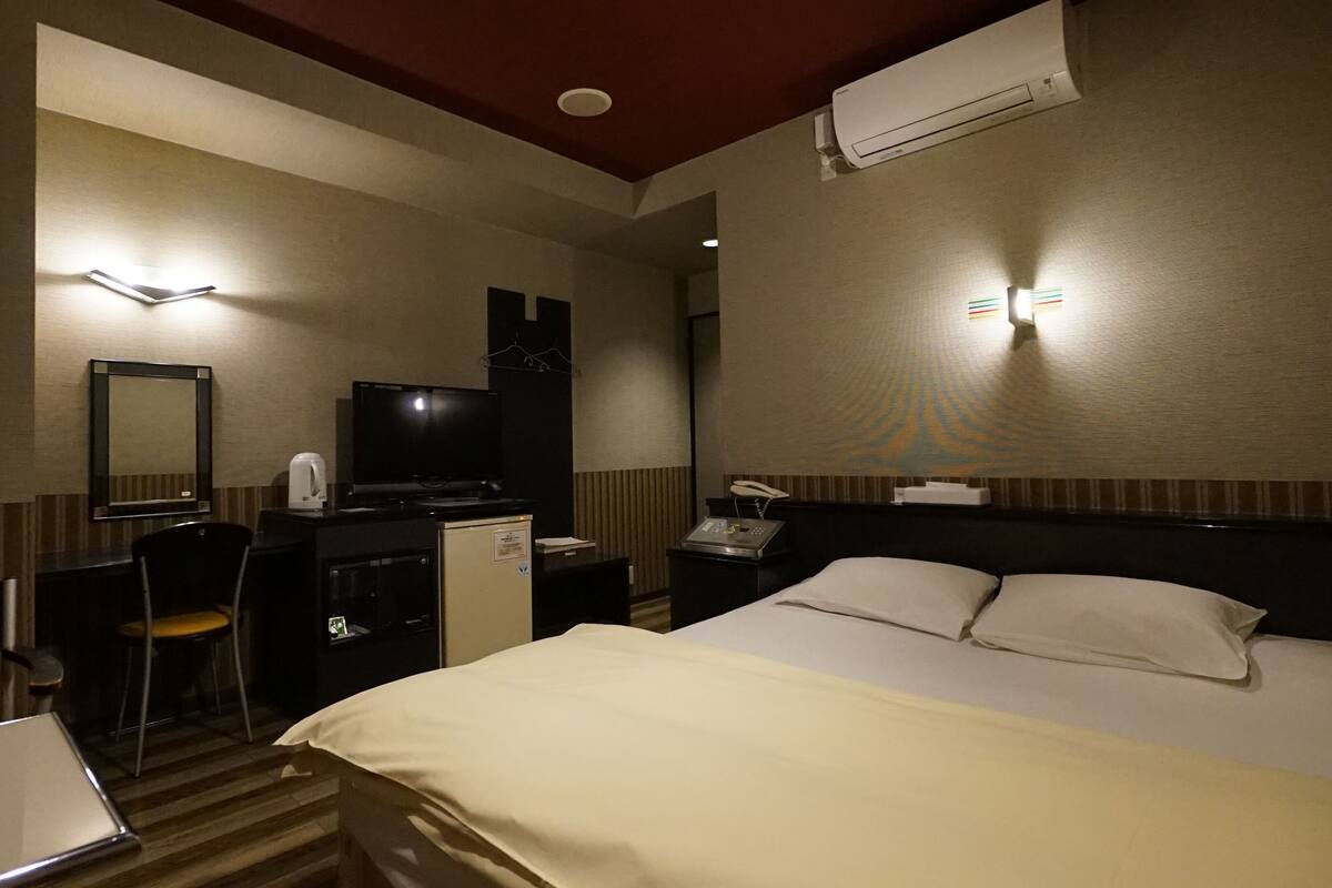 Quarto de hotel com uma cama, uma escrivaninha com computador, televisão e telefone.