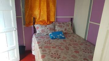 Quarto com cama, paredes roxas, cabeceira de madeira e janela com cortina.