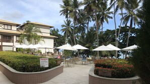 Pátio de resort com área de estar externa, palmeiras e piscina.