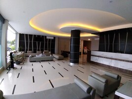 Um lobby moderno com uma mesa de recepção, área de estar e um pilar grande.