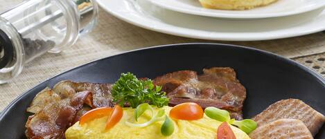 Prato de pequeno-almoço com ovos, bacon e salsicha, e outro prato com waffles e geleia.