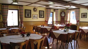 Uma sala de jantar com várias mesas e cadeiras, piso de madeira e cortinas xadrez.