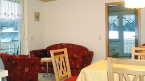 Uma sala de jantar com mesa e cadeiras, um sofá vermelho estampado e teto de madeira.
