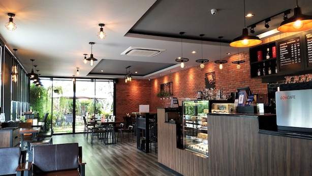 Interior de um café moderno com piso de madeira, paredes de tijolo e uma vitrine de vidro.