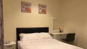 Uma cama bem arrumada com lençóis brancos, uma cabeceira preta, uma mesa de cabeceira com abajur, uma cadeira e duas pinturas penduradas na parede.