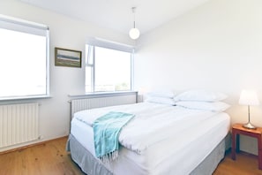 Quarto com cama, mesa de cabeceira com abajur, janela e radiador.