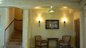Um hall com escada, duas poltronas, uma pequena mesa e uma obra de arte emoldurada na parede.