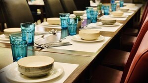Um restaurante com uma mesa longa posta para refeições, com copos azuis e pratos brancos.