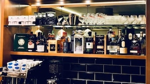 Uma área de bar com prateleiras cheias de garrafas e copos, uma máquina de café e um espaço com xícaras.