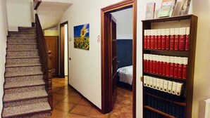 Uma escada leva a um quarto com uma cama, uma estante de livros e um quadro na parede.