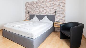 Quarto moderno com cama cinza, cabeceira com padrão de tijolos, poltrona de couro preto e mesa de cabeceira de madeira.