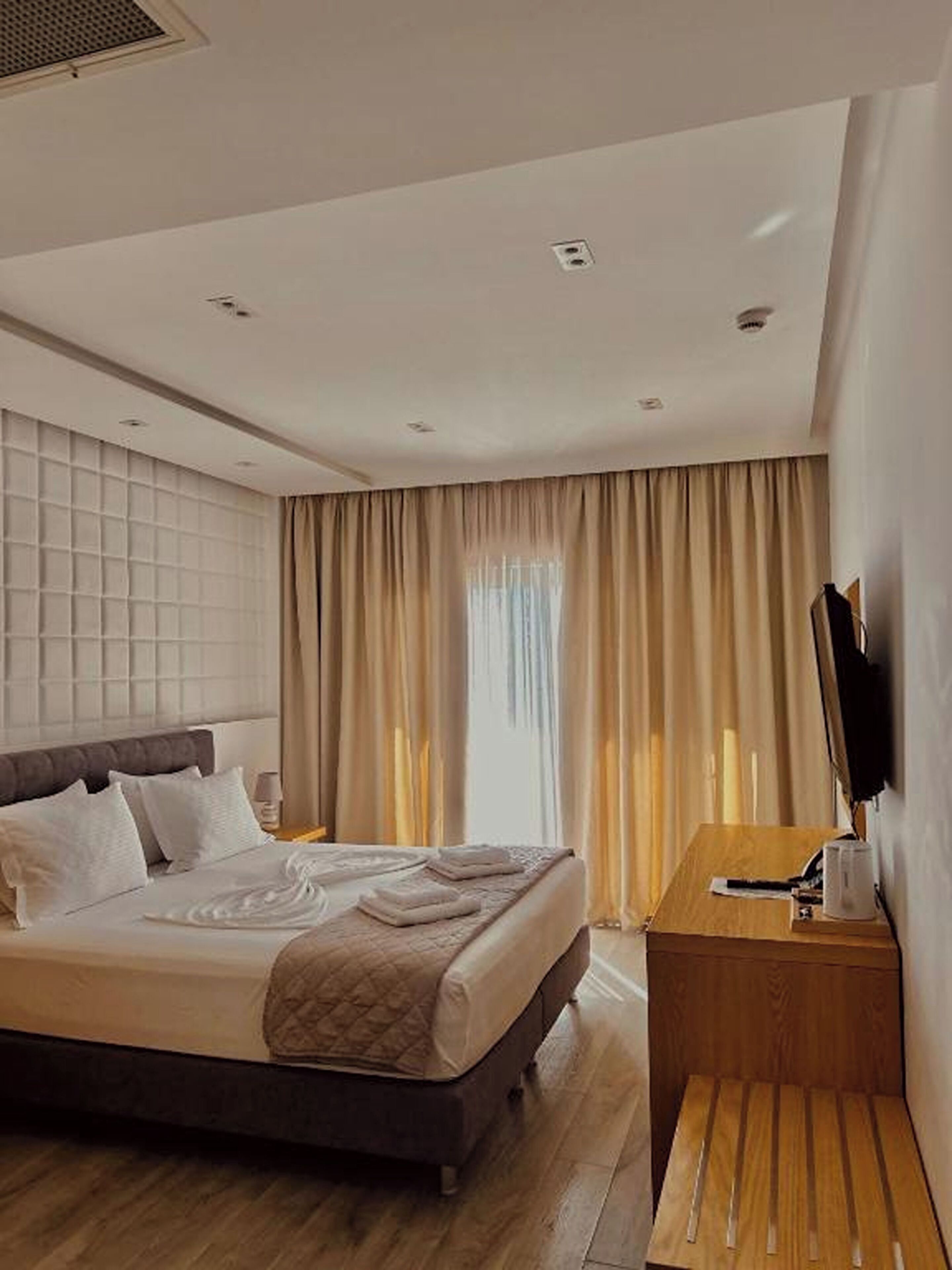 Quarto de hotel com cama, escrivaninha, televisão e janela com cortinas.