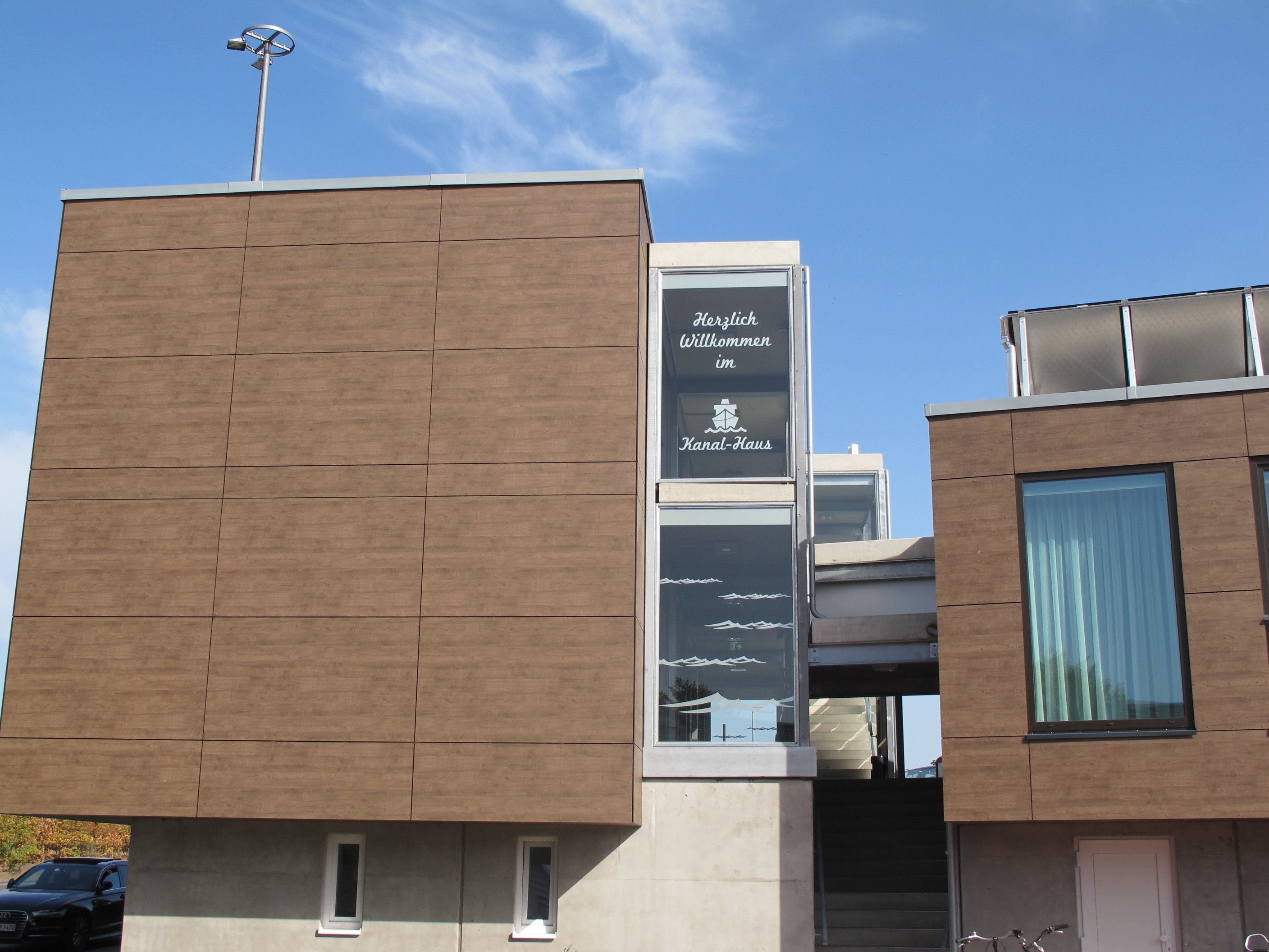 Um edifício moderno com uma placa que diz “Herzlich Willkommen im Kanal-Haus”, indicando uma mensagem de boas-vindas.