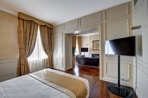 Quarto de hotel com uma cama grande, televisão de tela plana e vista para a sala de estar.