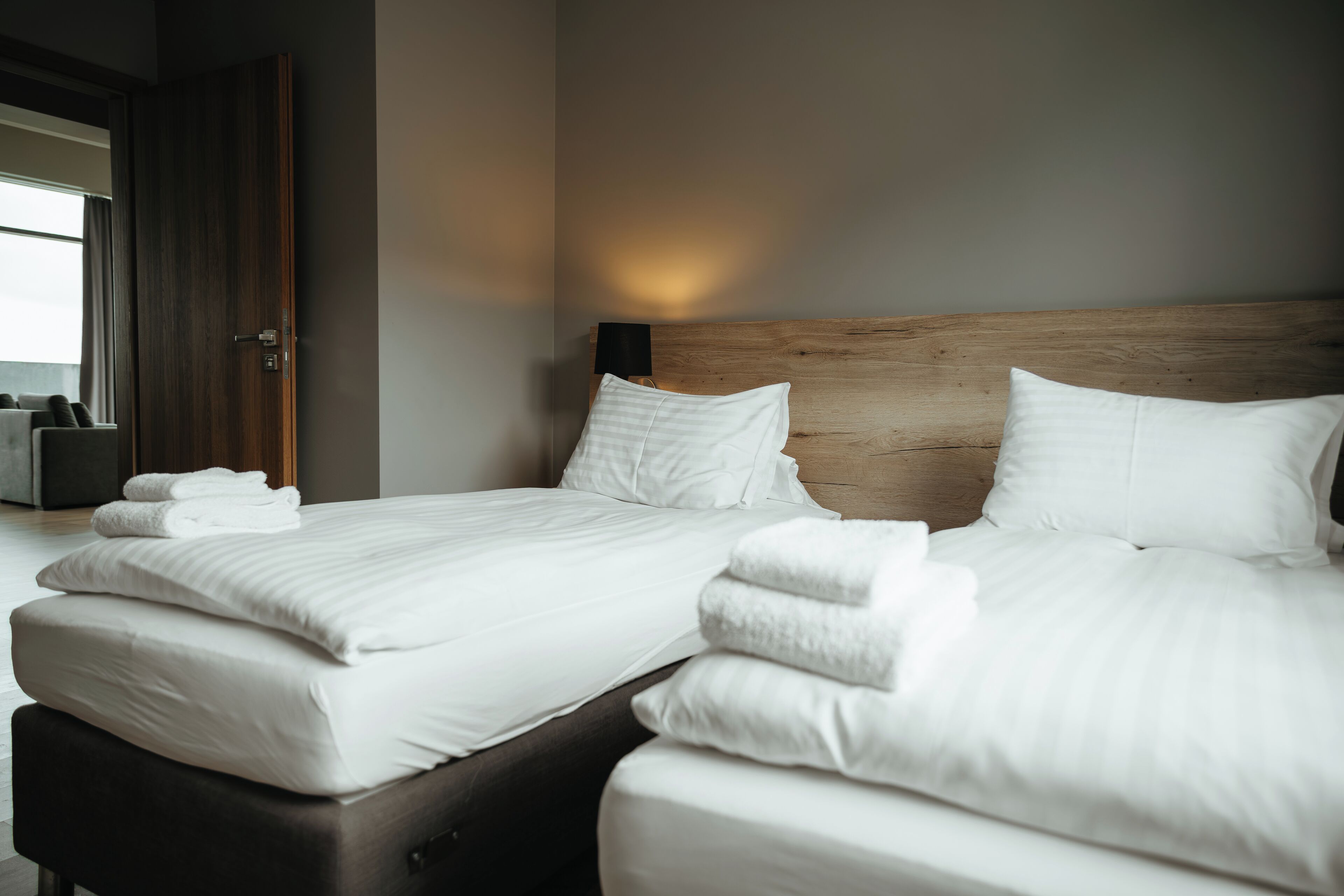 Quarto de hotel com duas camas, uma cabeceira de madeira e um abajur.