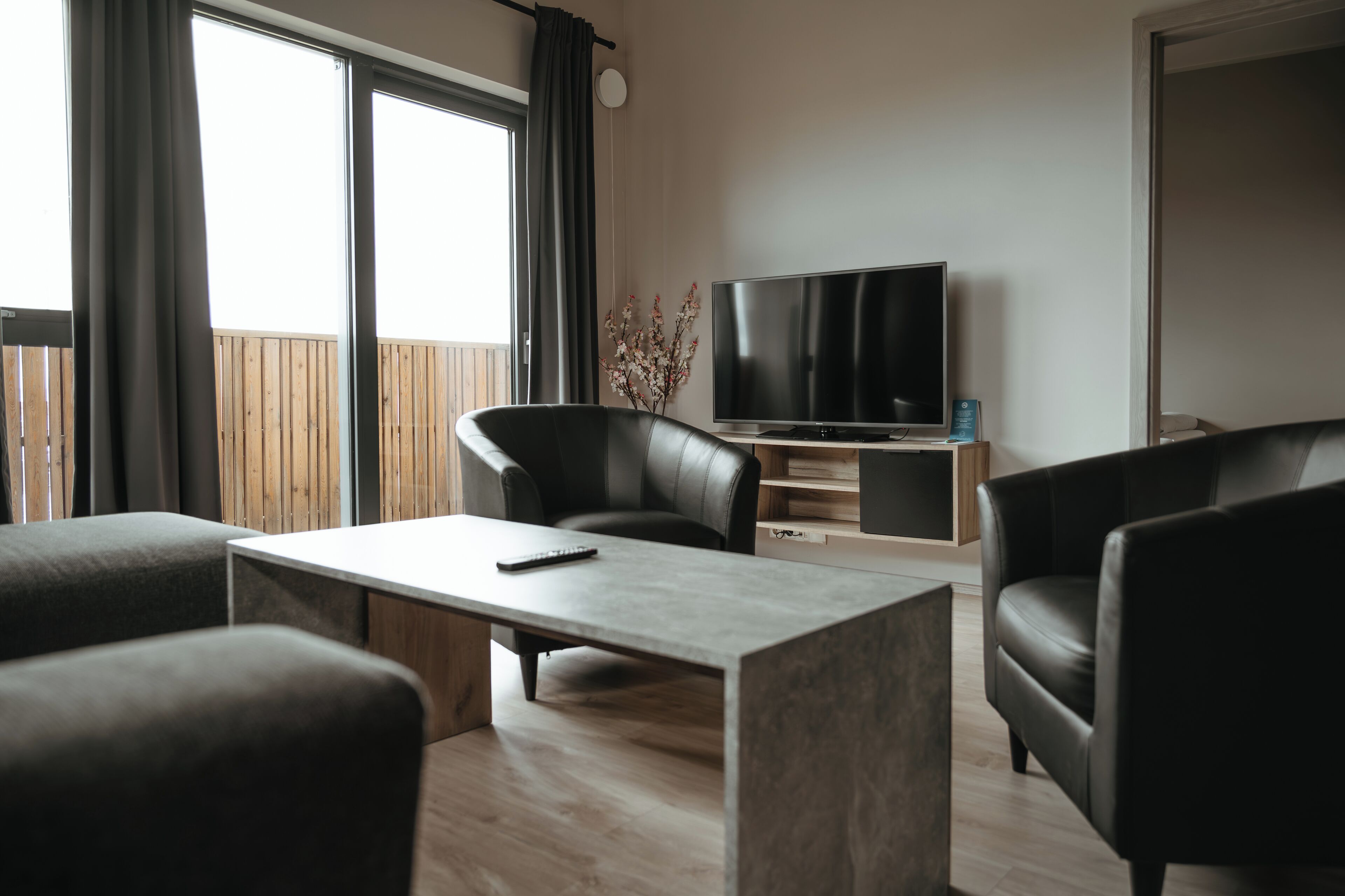 Uma sala de estar moderna com uma televisão de tela plana, dois sofás de couro preto, uma mesa de centro e piso de madeira.