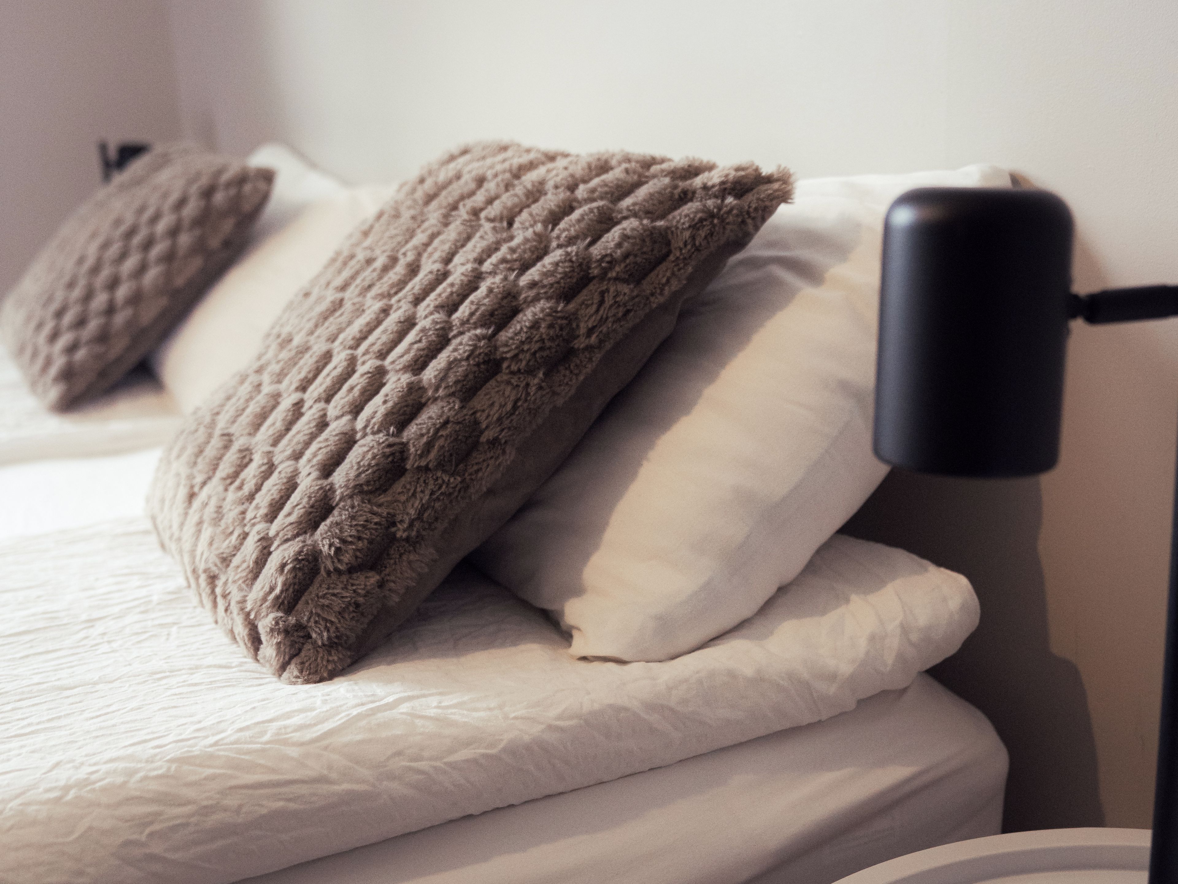 Cama com roupa de cama branca e duas almofadas texturizadas.