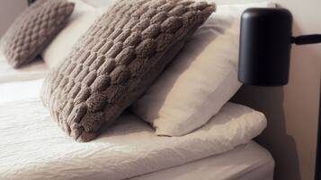 Cama com roupa de cama branca e duas almofadas texturizadas.