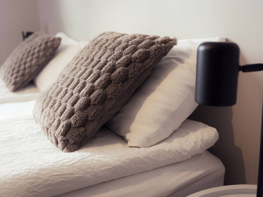 Cama com roupa de cama branca e duas almofadas texturizadas.