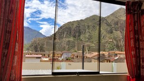 Quarto com grande janela com vista para paisagem montanhosa com campos em socalcos e edifícios tradicionais.