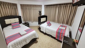 Quarto de hotel com duas camas, cortinas bege, uma televisão na parede e uma pequena mesa com um vaso de flores.