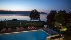 Piscina com espreguiçadeiras e vista para um lago ao entardecer.