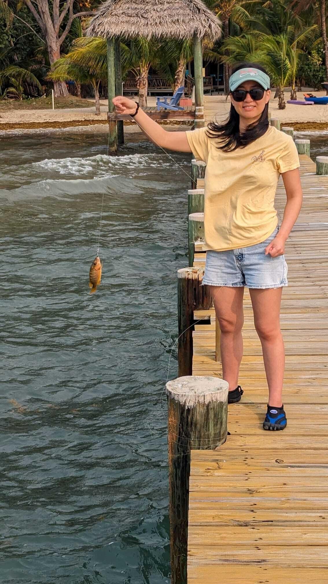 Uma pessoa em um cais de madeira que se estende sobre a água, segurando um peixe.